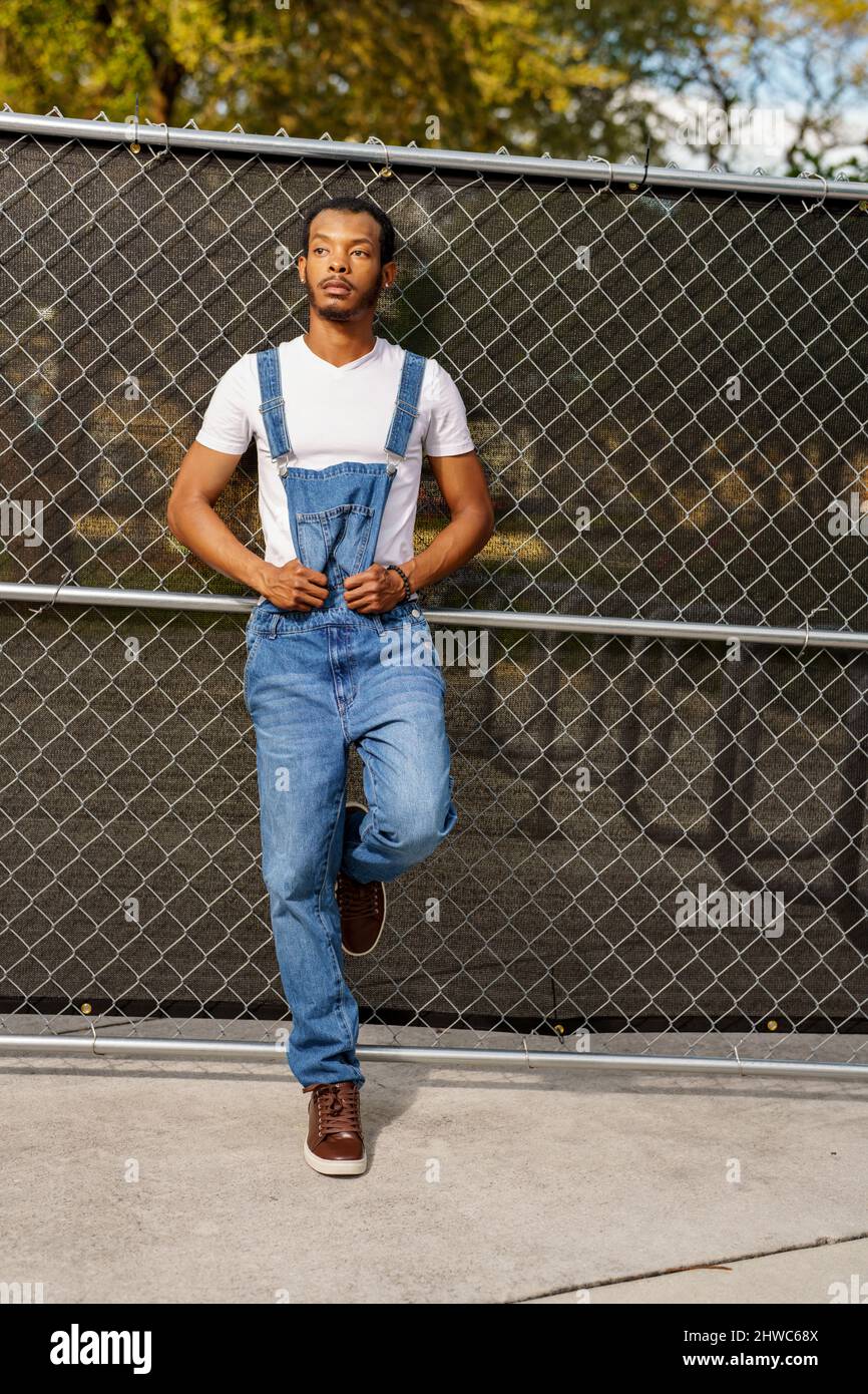 He is wearing overalls and leaning on a fence Stock Photo - Alamy