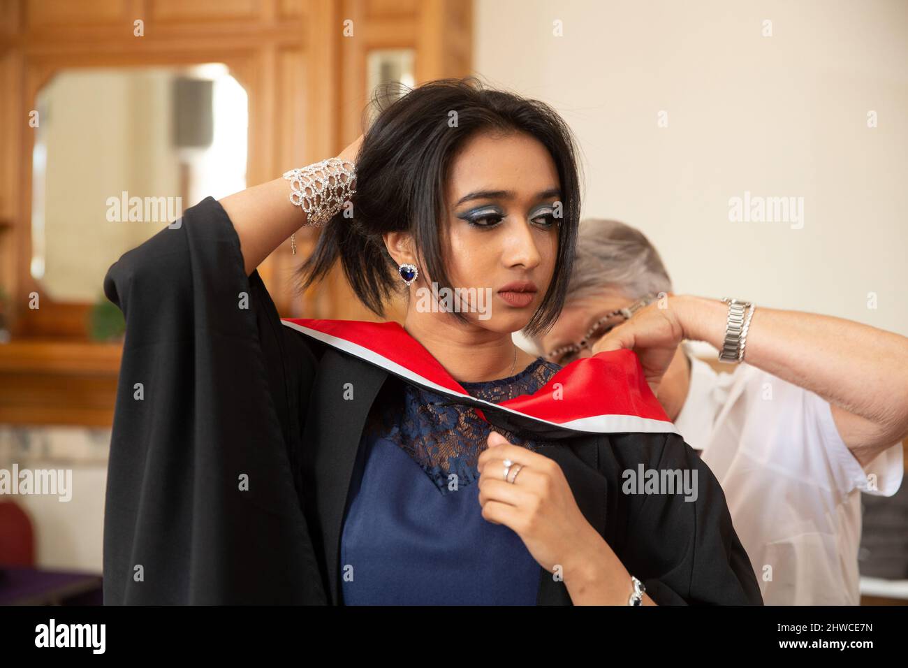 A pretty Asian female graduate getting her robe placed at her ...