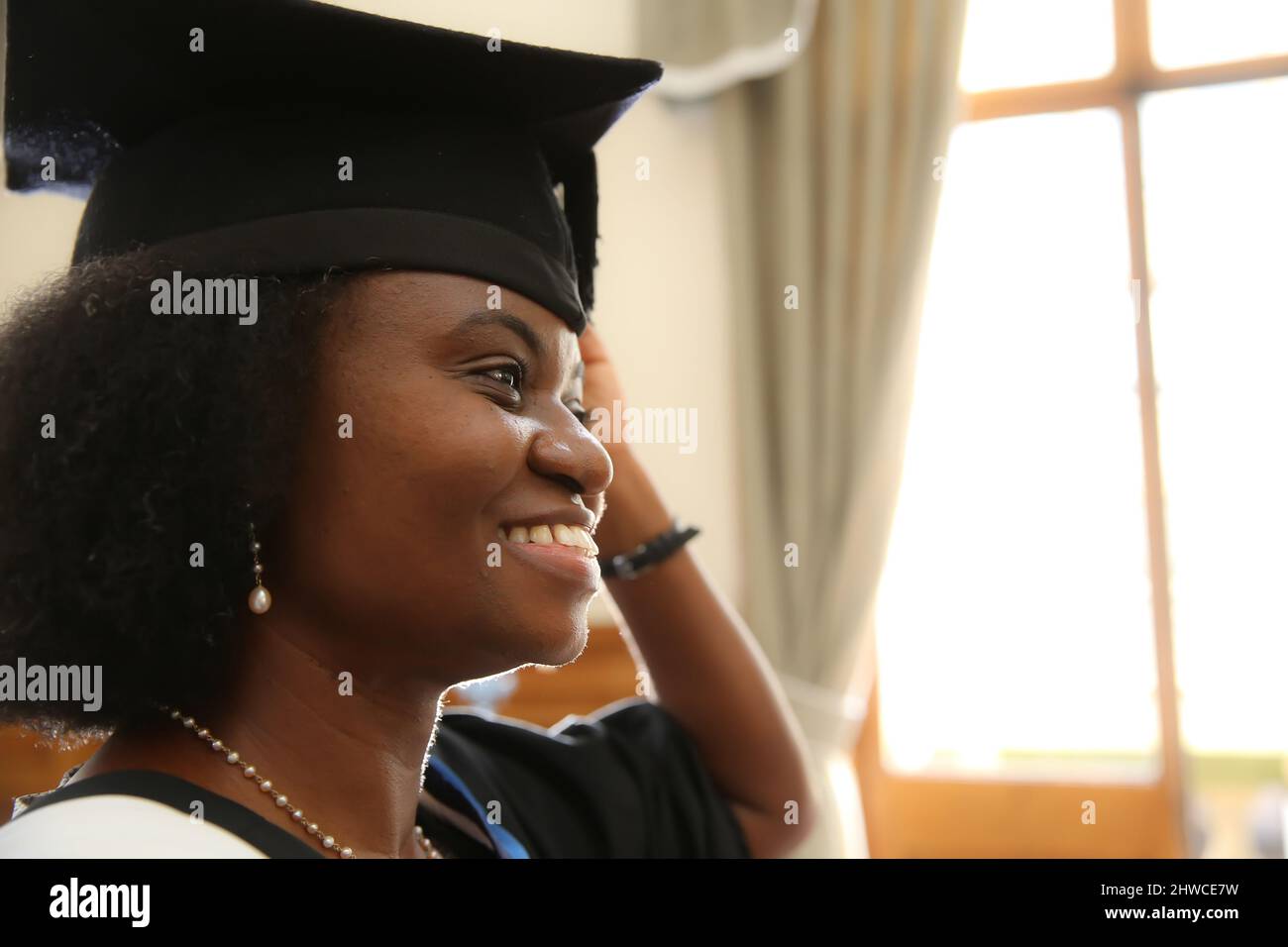 A pretty Afro-Caribbean female graduate trying on her mortarboard at ...