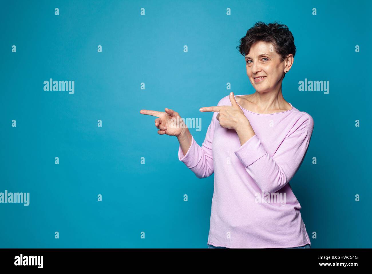 Mid adult woman smiling and pointing finger on blue studio background ...