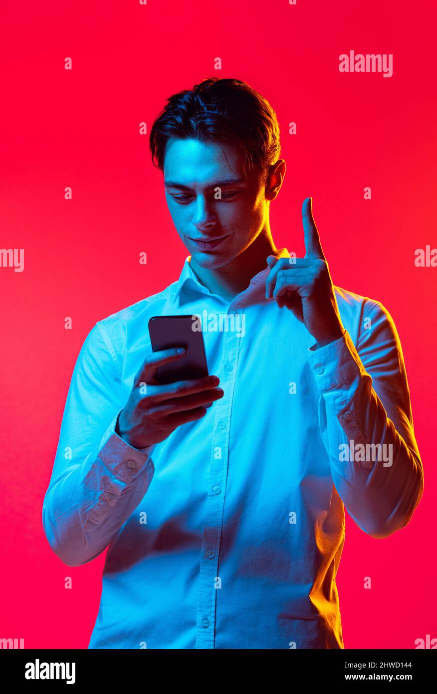 Portrait of young man, student looking on phone and rising finger up ...