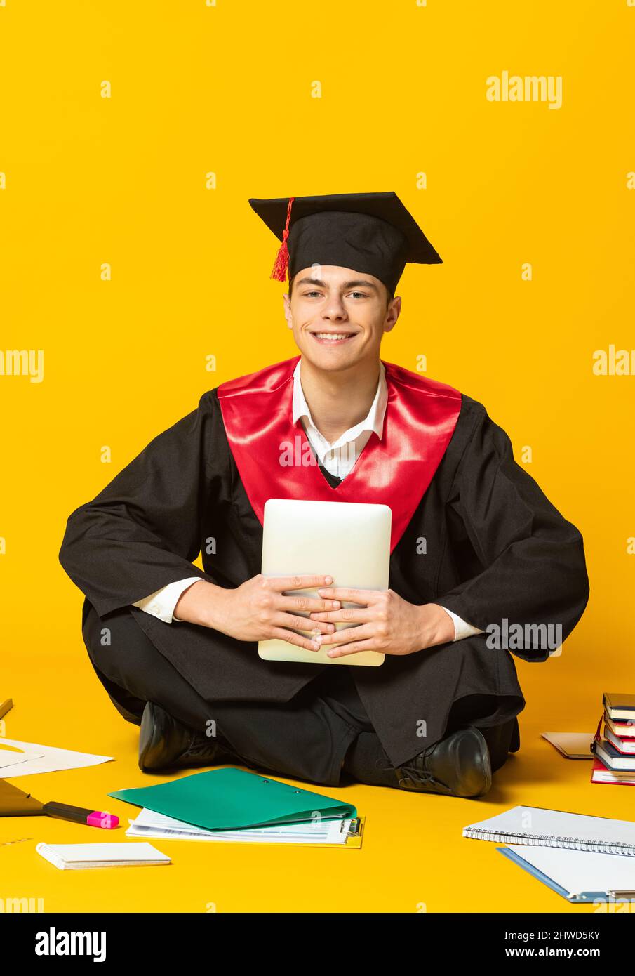 Portrait of young man, student in graduation cap and gown sitting on ...