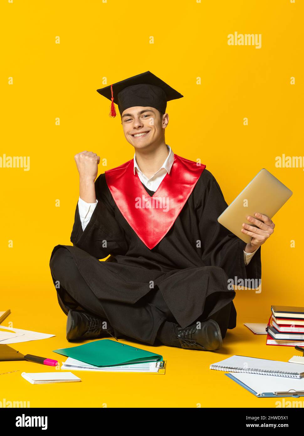 Portrait of young man, student in graduation cap and gown sitting on ...