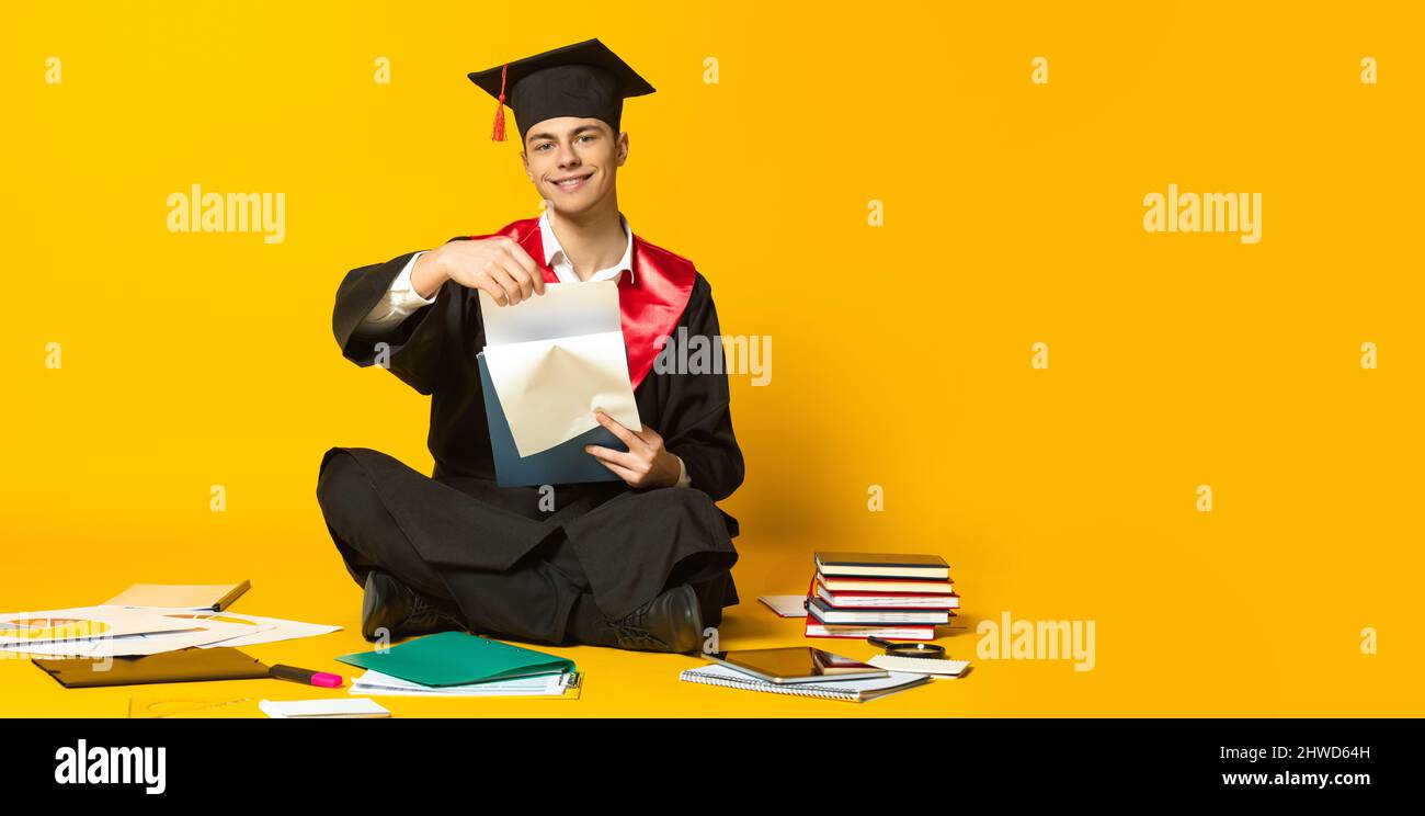 Portrait of young man, student in graduation cap and gown sitting on ...