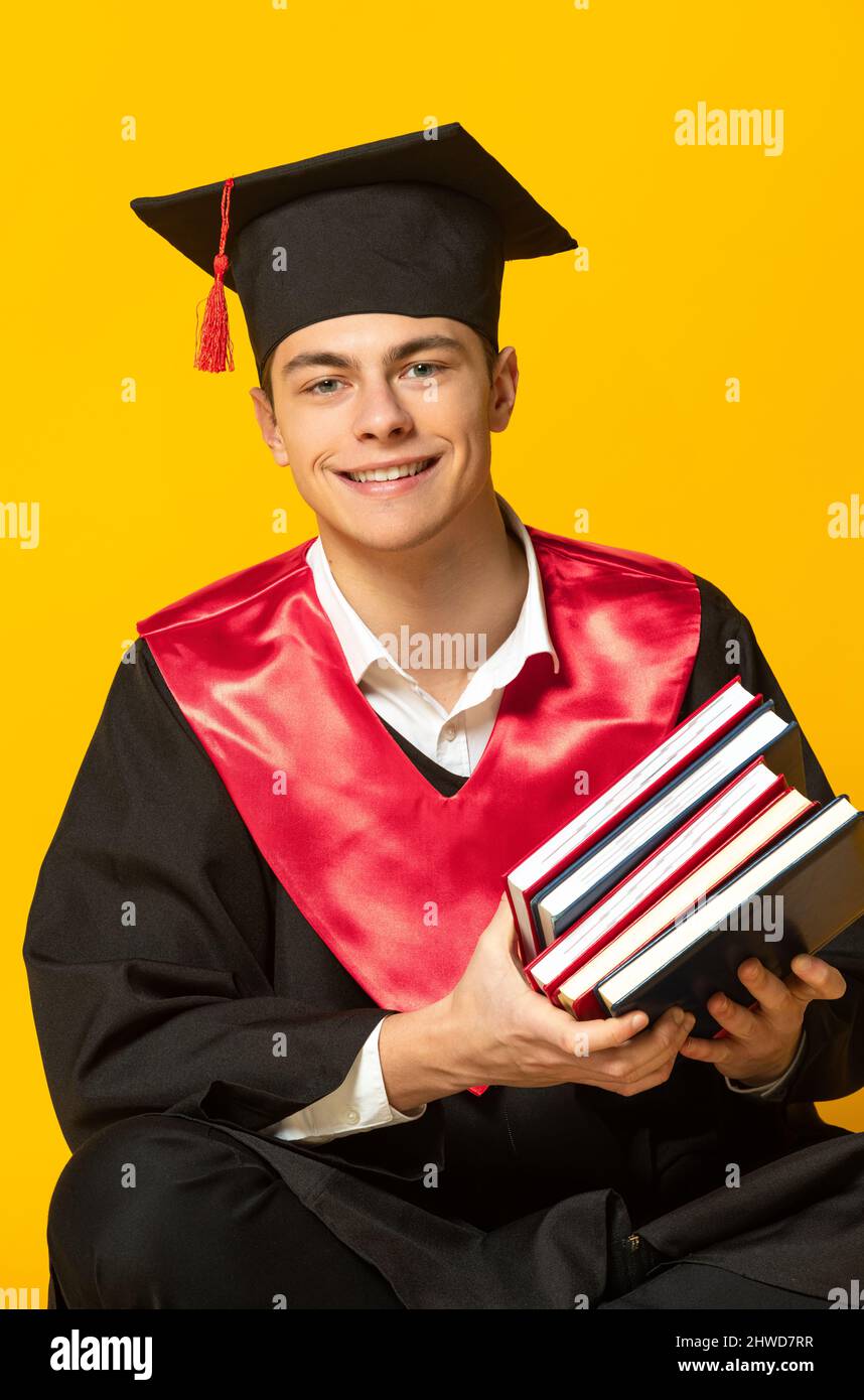 Portrait of young smiling man, student in graduation cap and gown with ...
