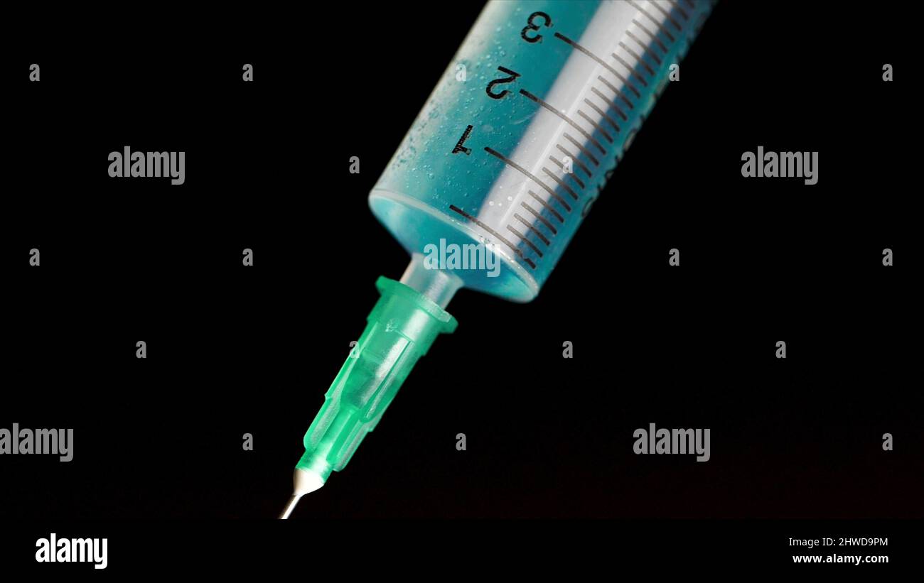 Taking vaccine into a glass syringe from a ampule on a black background ...