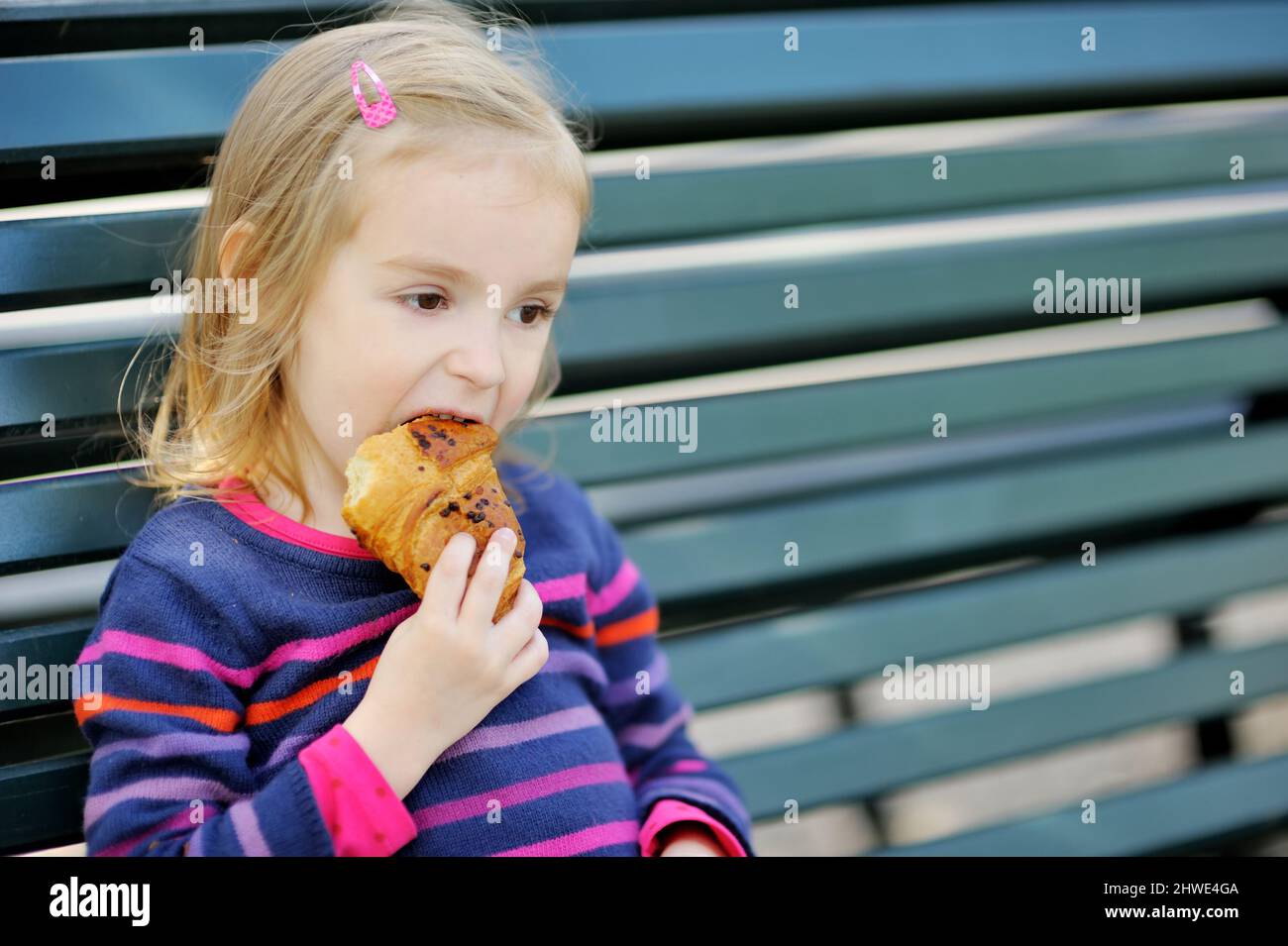 Adorable little girl eating fresh baked croissant while sitting on a ...