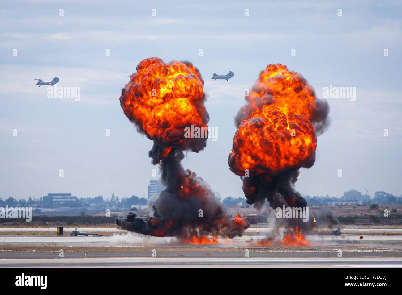 Bomb explosion at an airfield with combat helicopters in the background ...