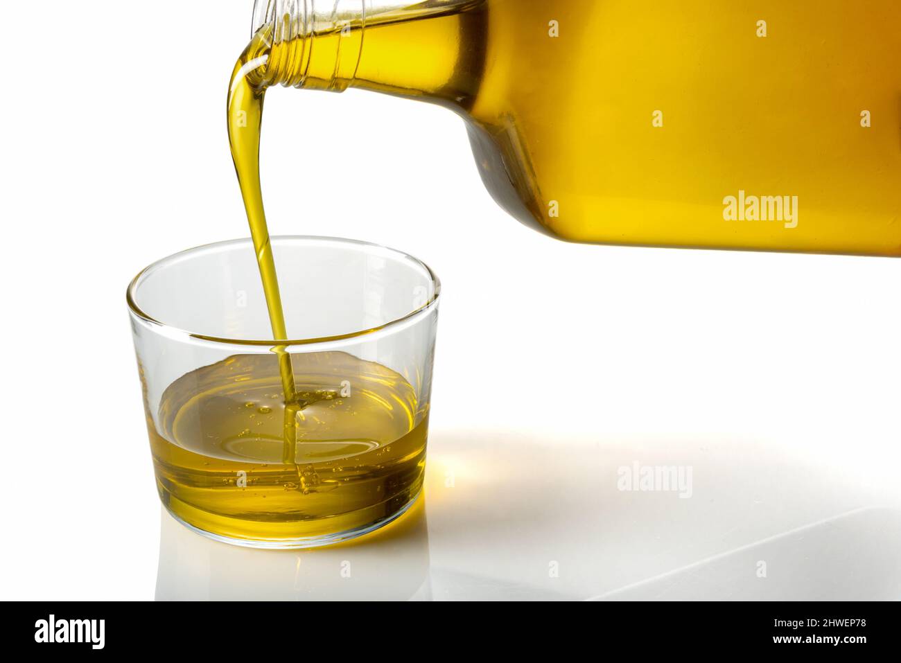 Extra virgin olive oil being poured from bottle into glass cup on white ...