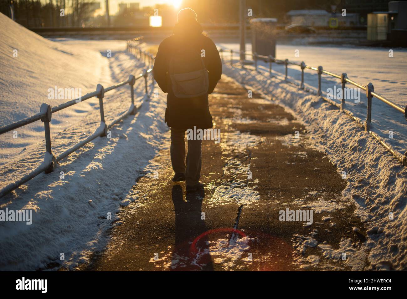 Man walks down road into sunset. Sun is setting. Pedestrian in winter ...