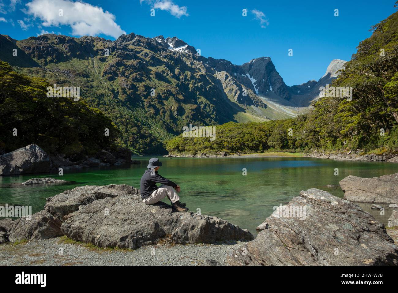 A man sitting on the rocks by the Lake Mackenzie, Routeburn Track ...
