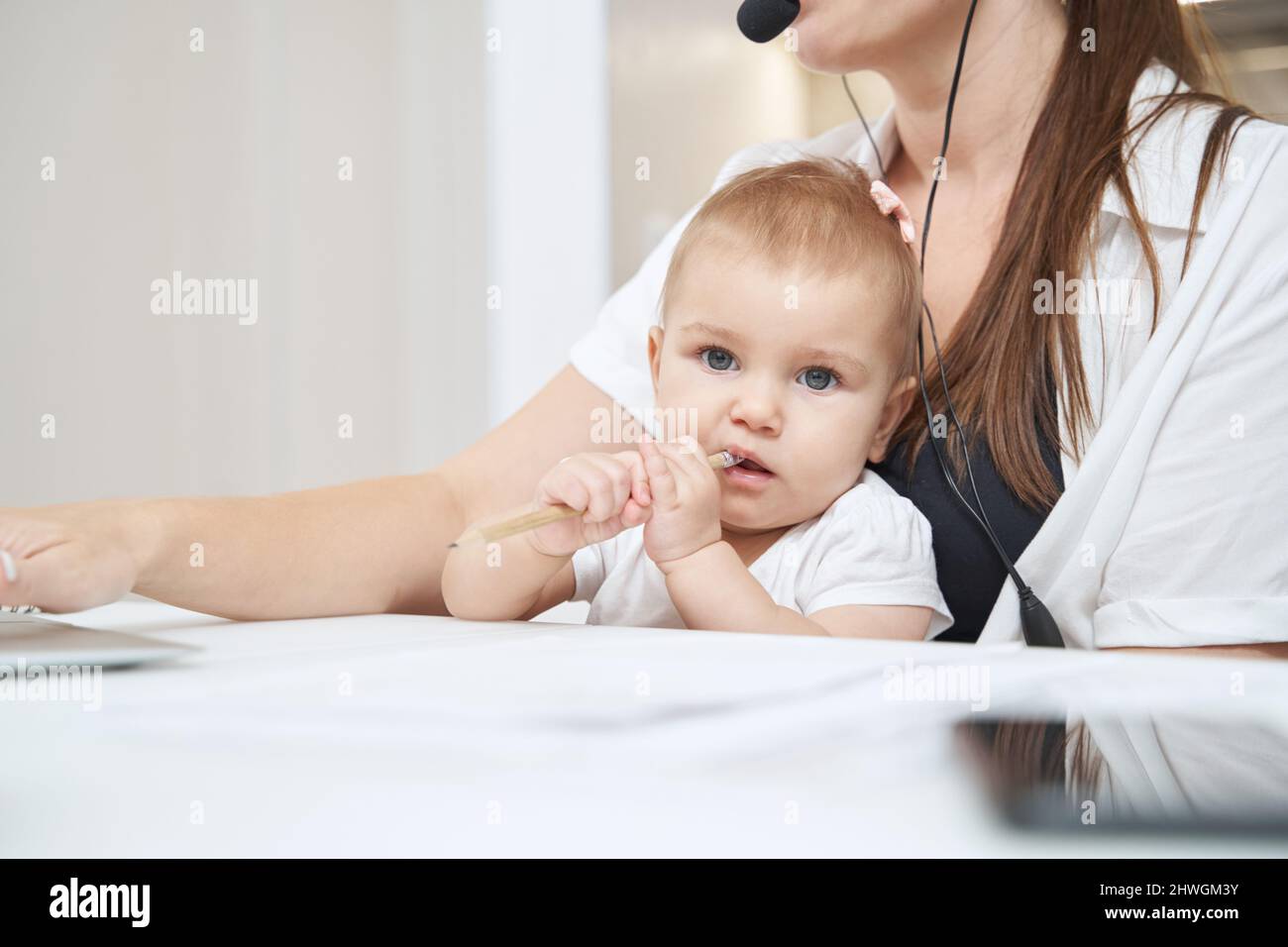 Baby biting pencil tip while sitting on mother knees Stock Photo - Alamy