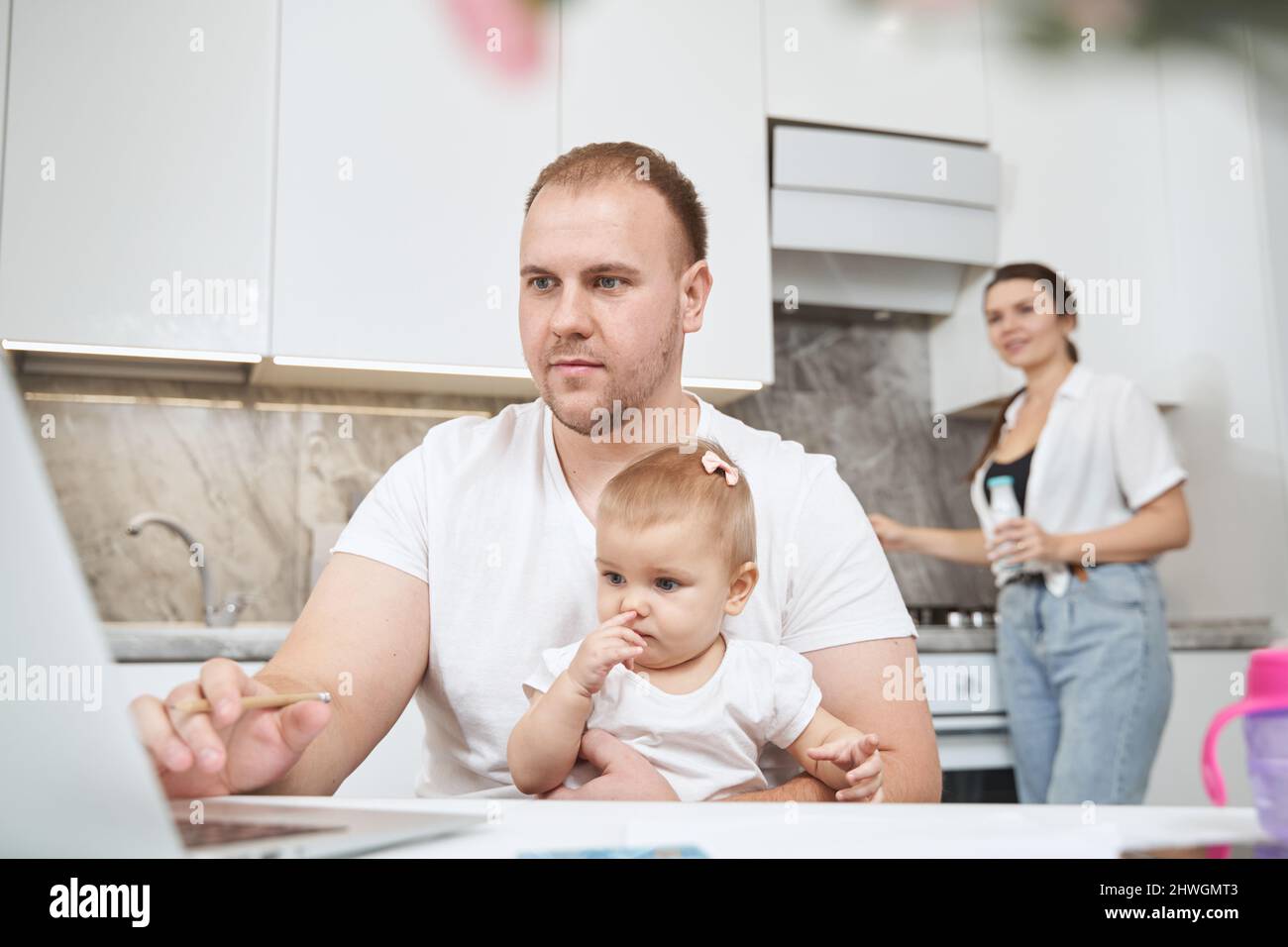 Busy father holding kid while working with laptop Stock Photo - Alamy