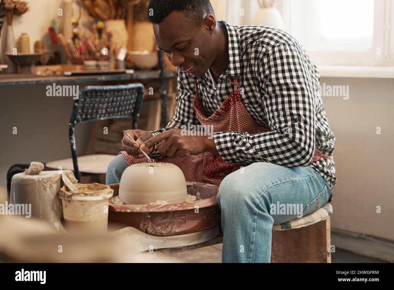 Cheerful ceramist removing excess clay on lower part of earthenware ...
