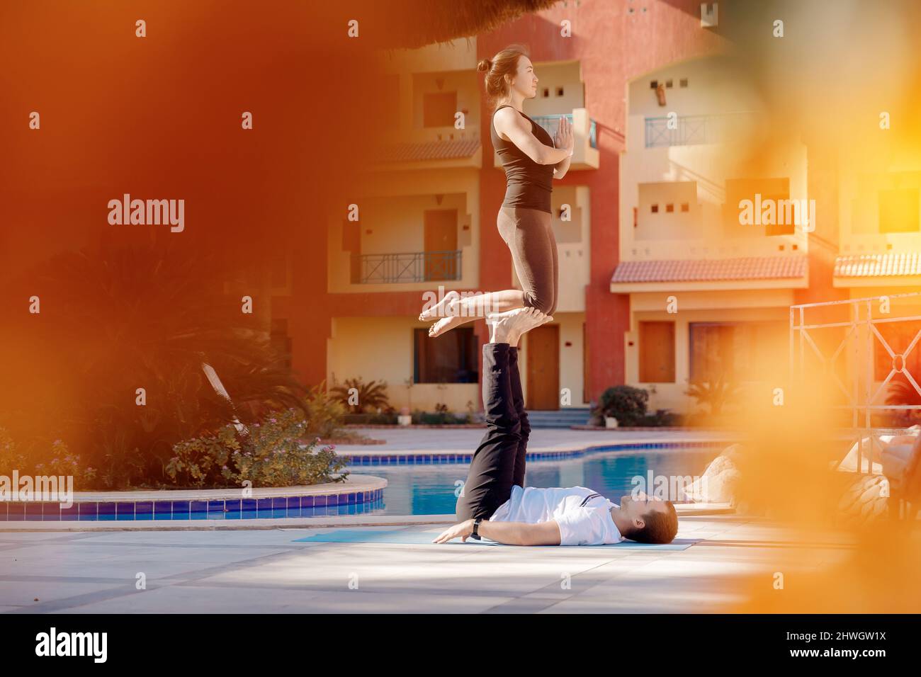 Happy couple lover young woman and man doing asana yoga background swimming pool palm trees and ...