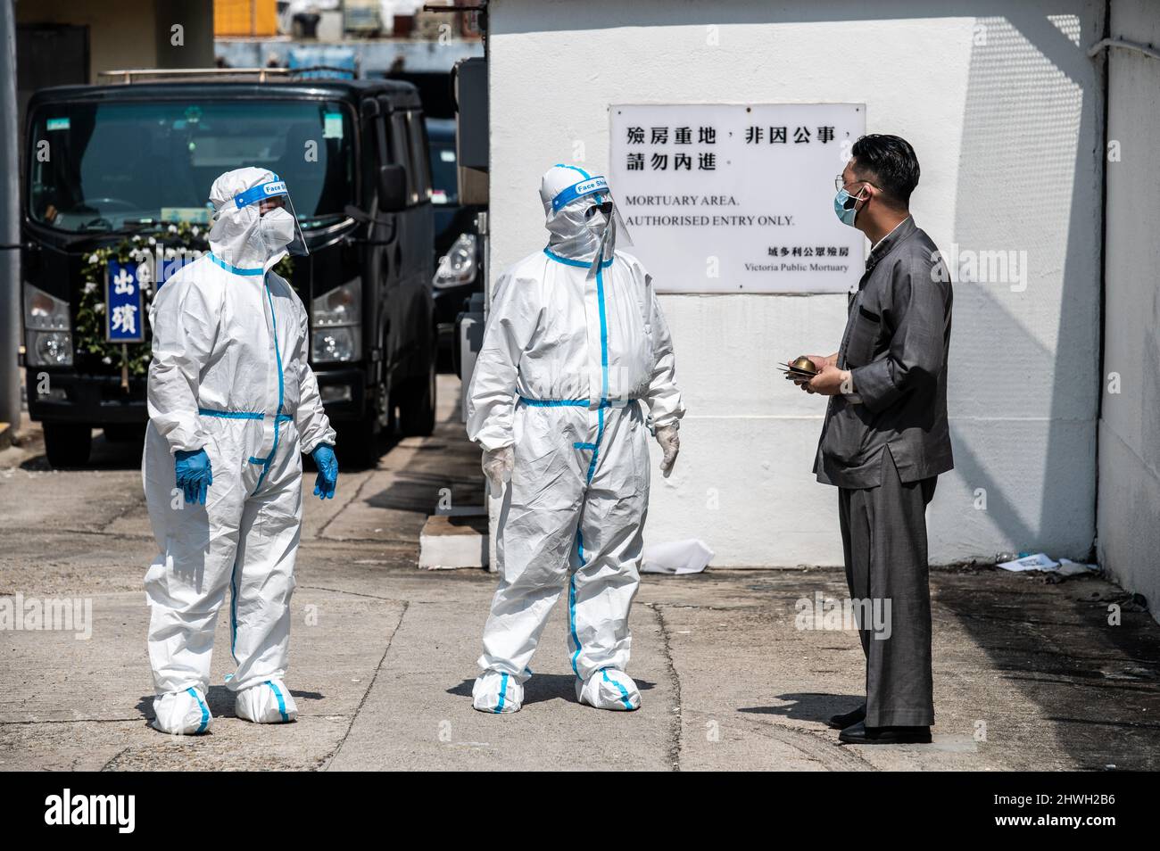 Private mortuary workers in full PPE discuss a funeral ceremony with a ...