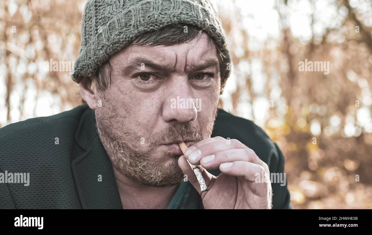 a poor homeless man with dirty hands smokes a cigarette in modern ...
