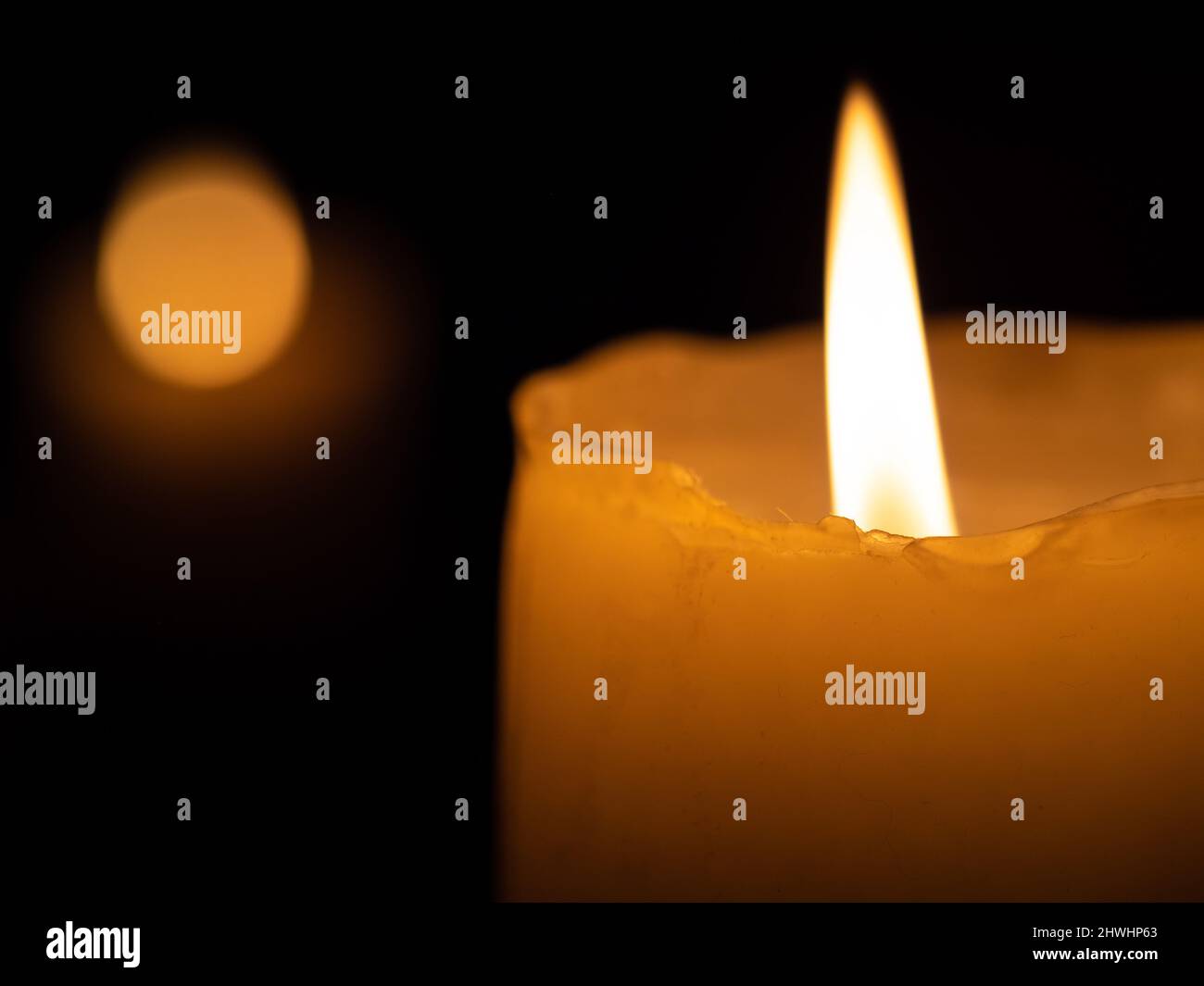Close-up thick lit candle very close to the right area of the photo and ...