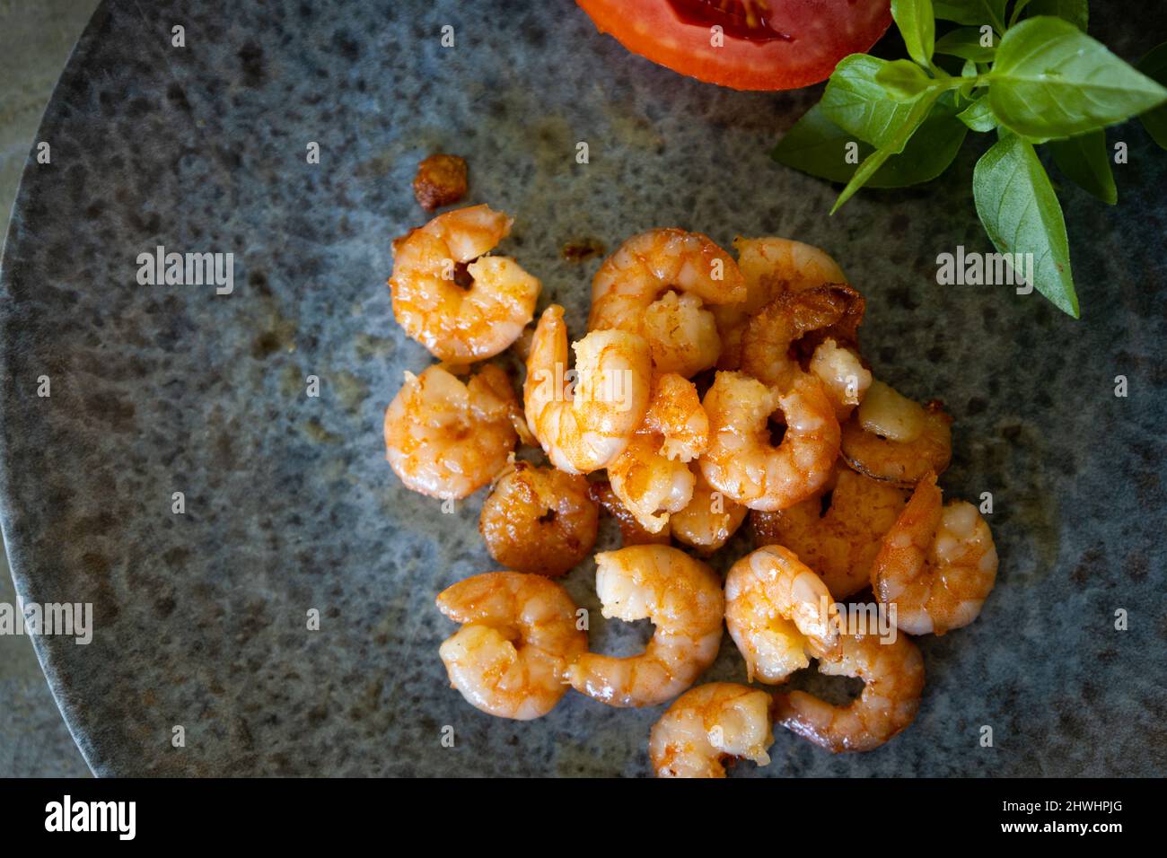 Delicious freshly cooked shrimp on a gray plate next to a tomato and ...
