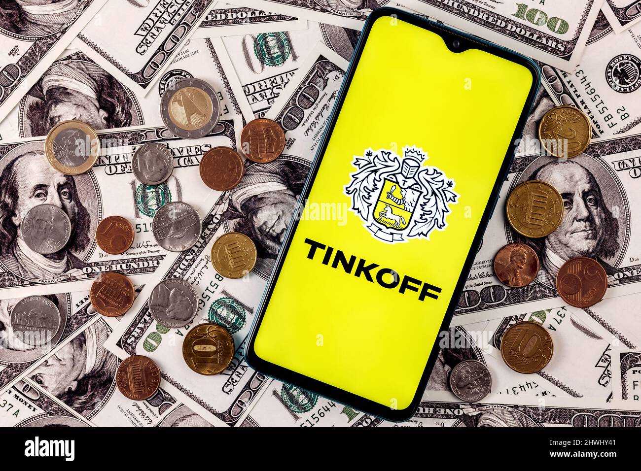 Smartphone with Tinkoff bank logo surrounded by variety of metal coins ...