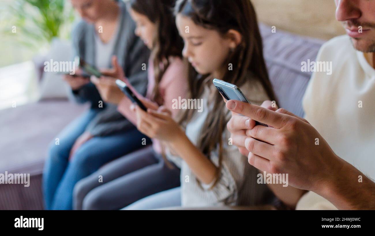 Family with two little daughters, everyone is using mobile phone in the ...