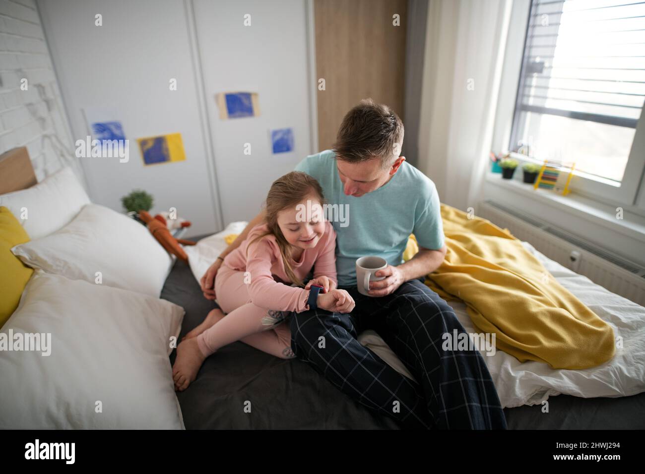 Father with his little daughter with Down syndrome sitting on bed and ...