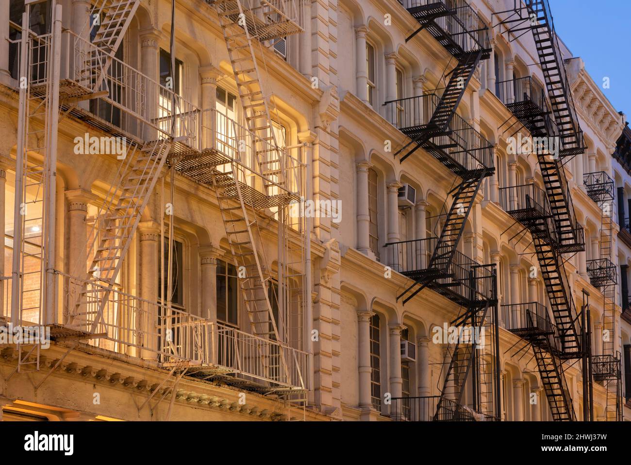 Facades of Soho loft buildings with fire escapes at dusk. Lower ...