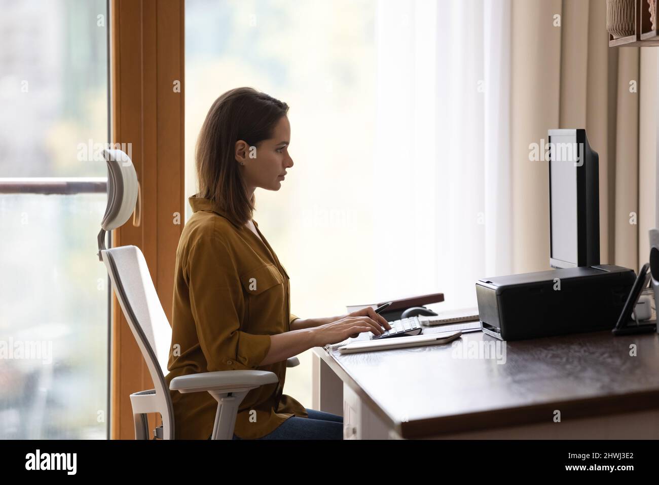Side view young woman sit at desk working on pc Stock Photo - Alamy