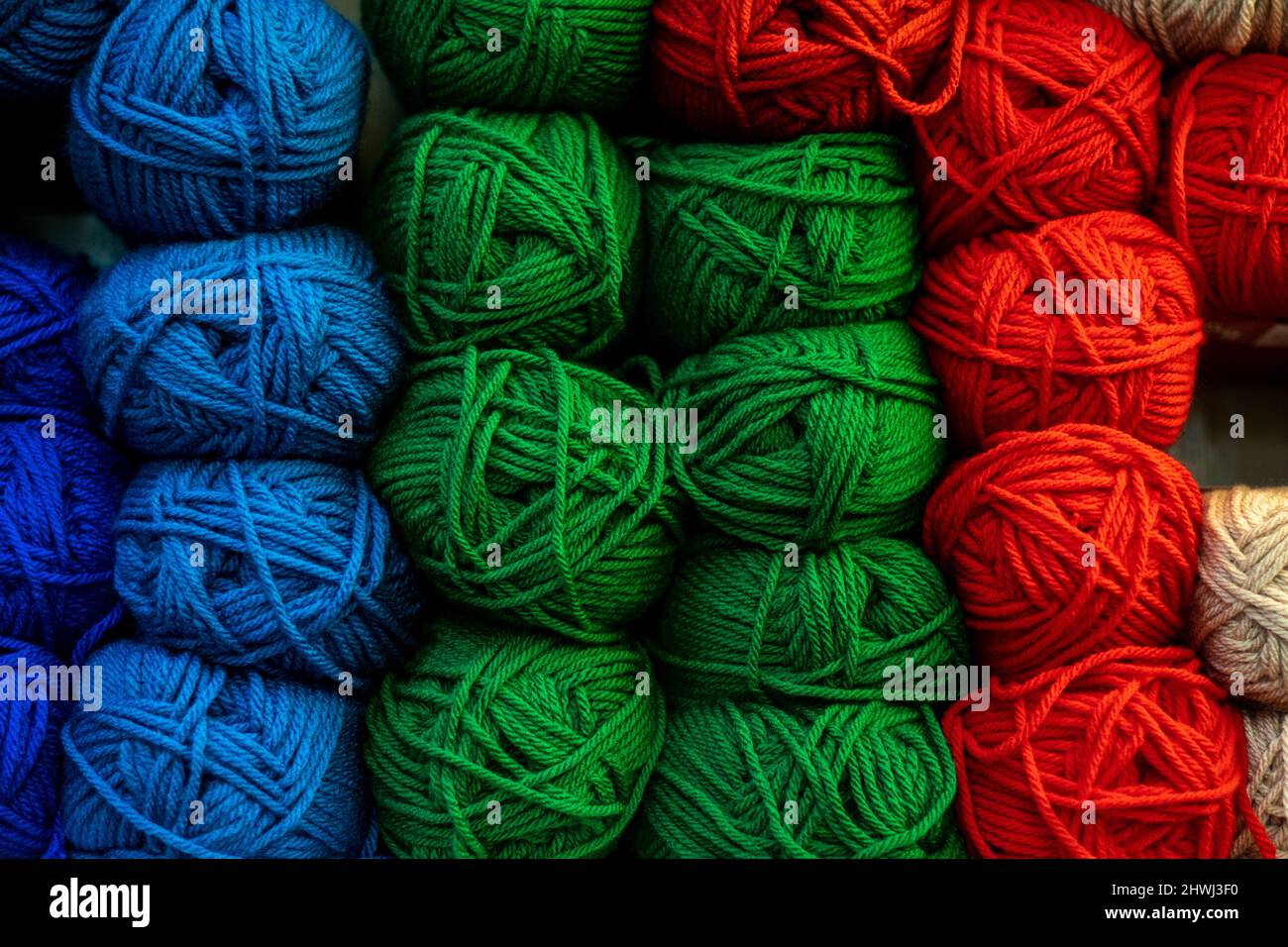 Many wool yarns in bright colours stacked on the shelf in store, rows ...