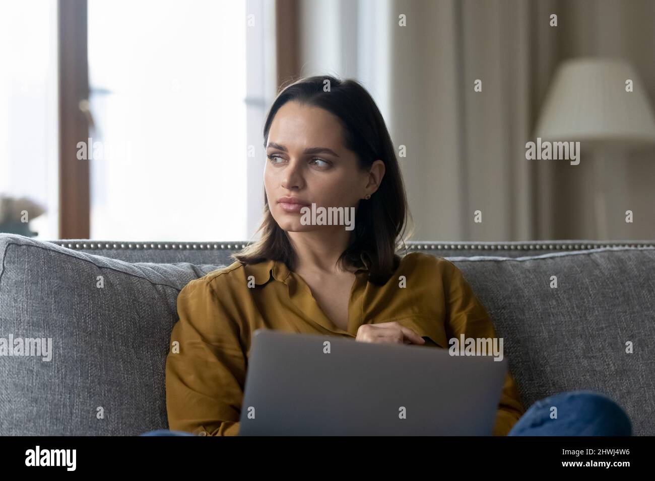 Woman sit on couch with laptop staring aside looking pensive Stock ...