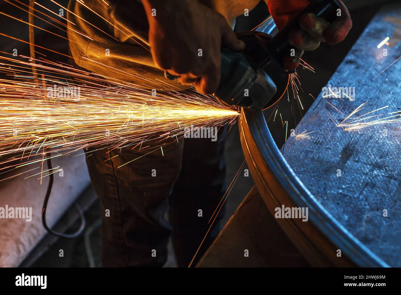 Heavy industry worker cutting steel with angle grinder in assembly shop ...