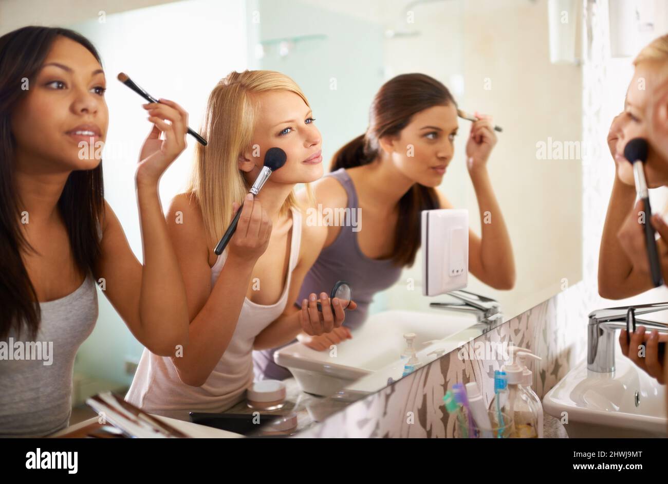 Beauty Queens. Shot of three friends applying makeup in front of the ...
