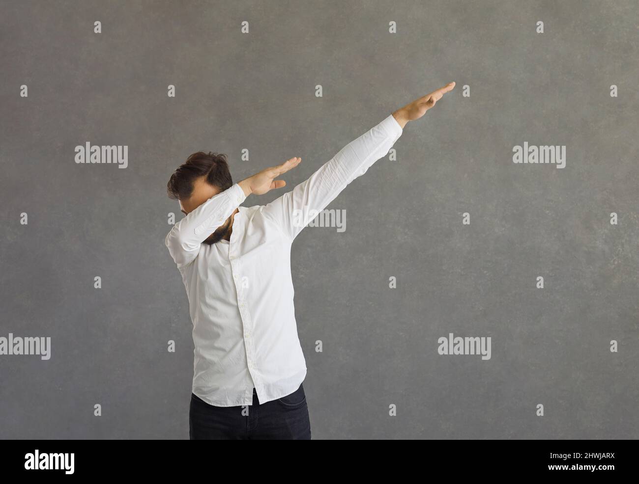 Happy young businessman doing a dab dance move standing on a grey ...