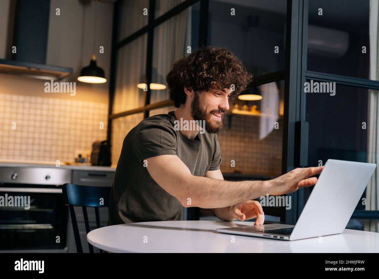 Side view of smiling young freelancer male opening laptop and starts ...