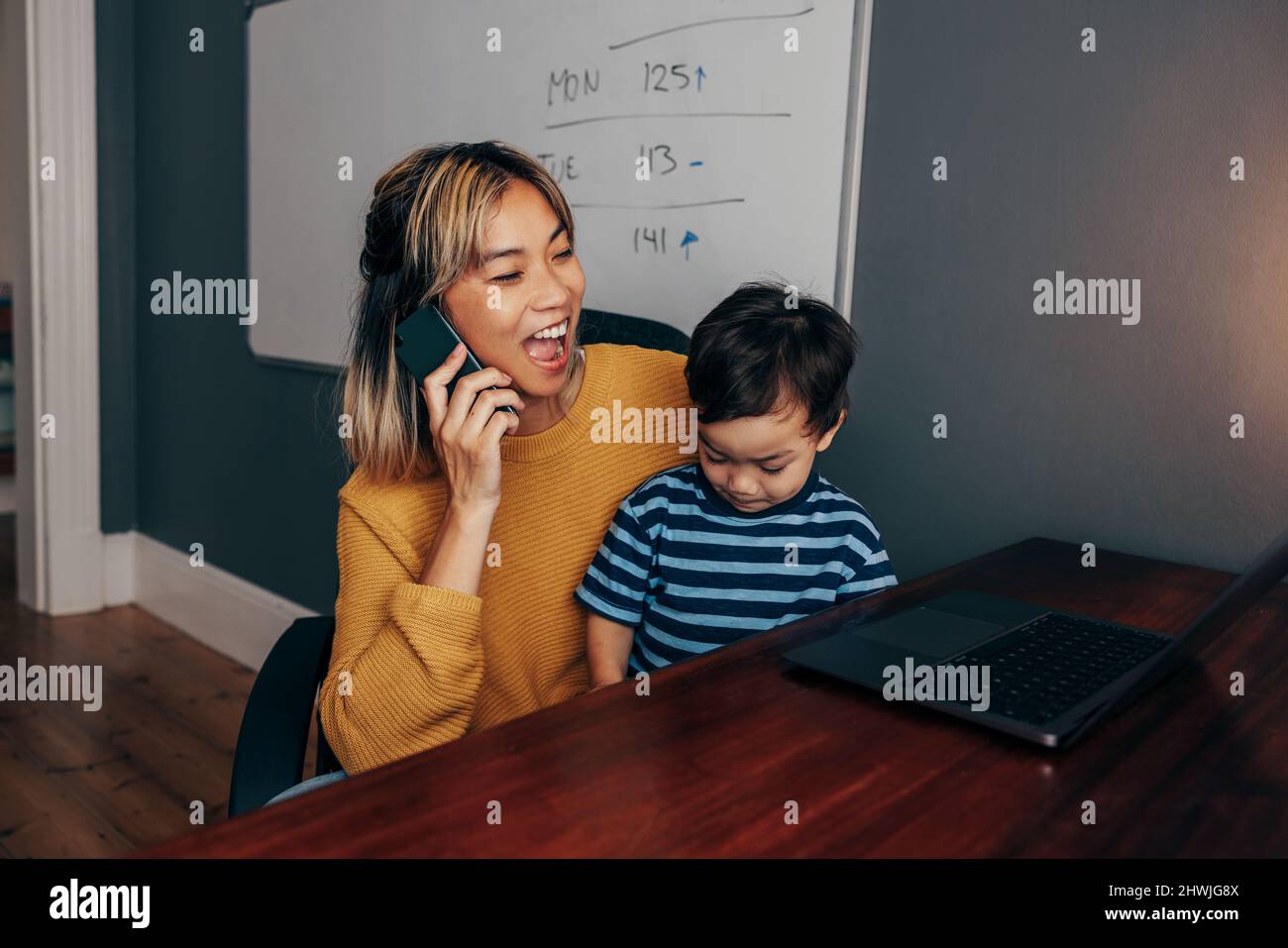Cheerful mom speaking on the phone while carrying her son on her lap ...