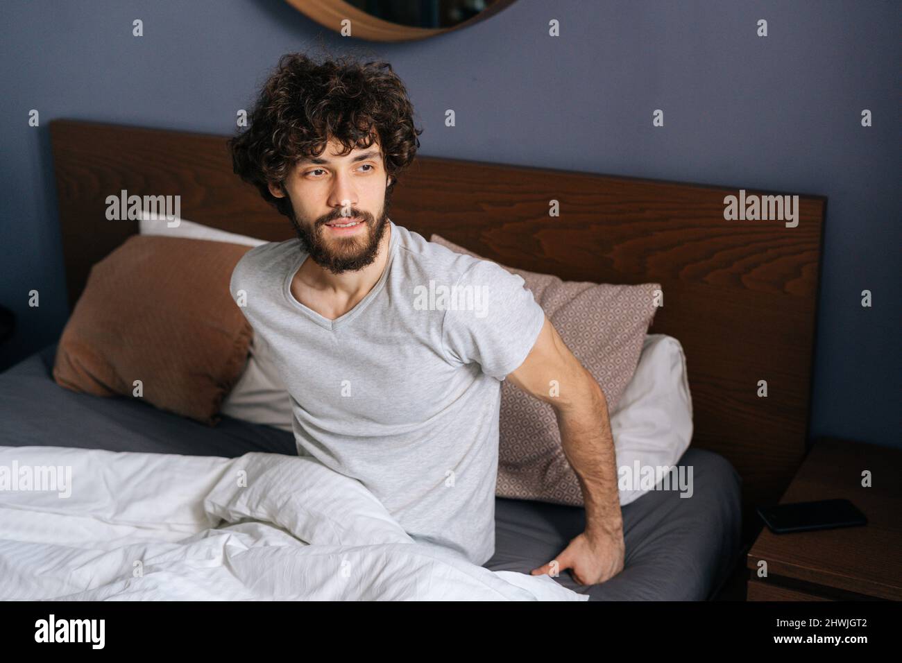 Portrait of handsome young man sitting on bed after waking up and ...