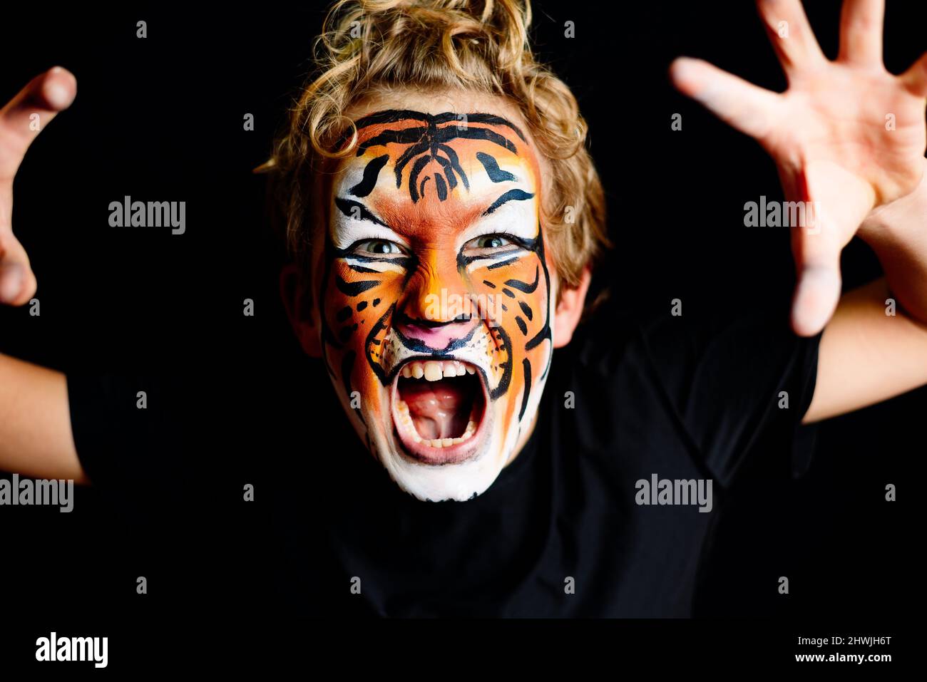 A growling boy with his face painted in the striking colors of a tiger ...