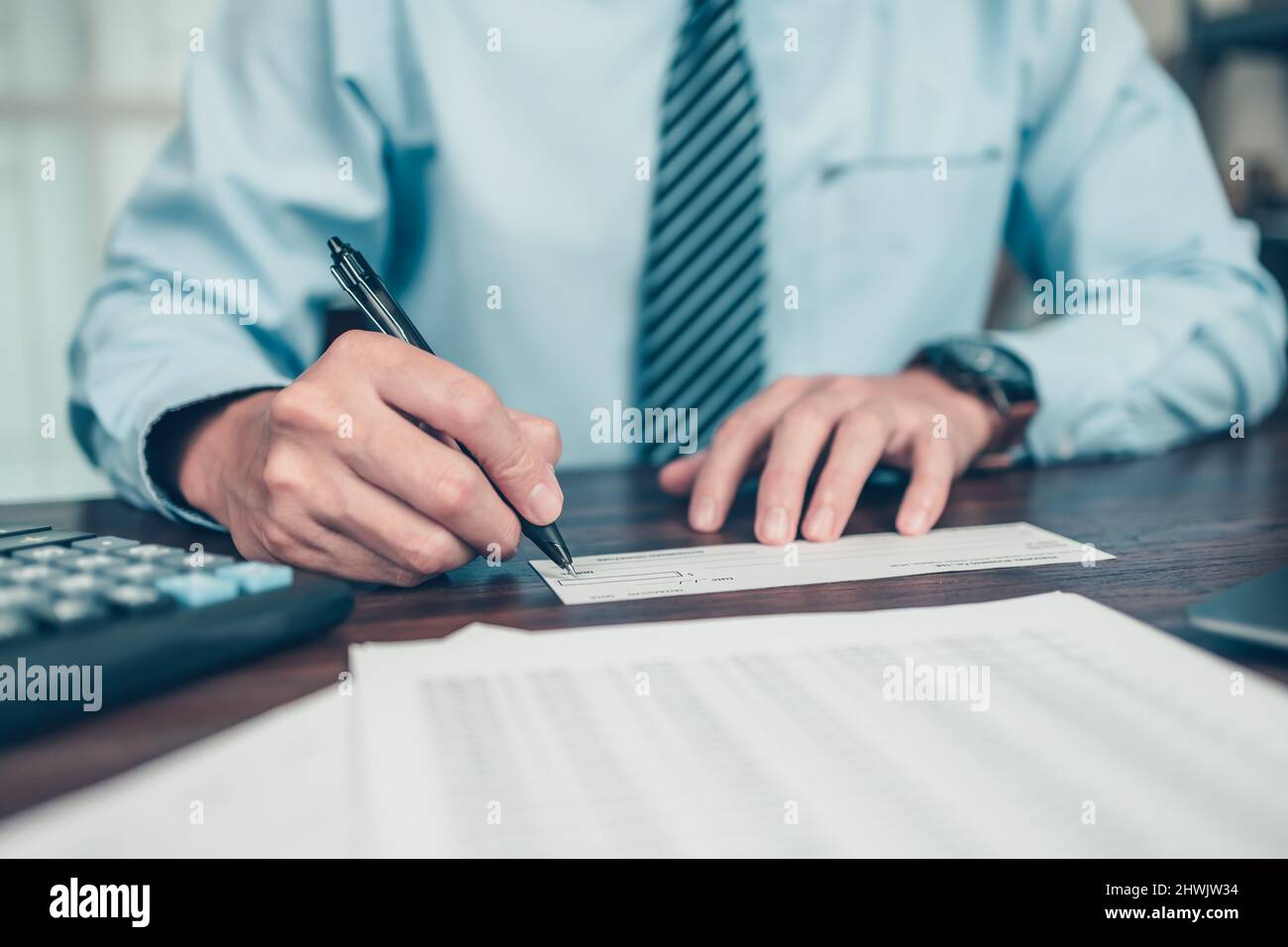Business man hand writing and signing white blank bank check book and ...