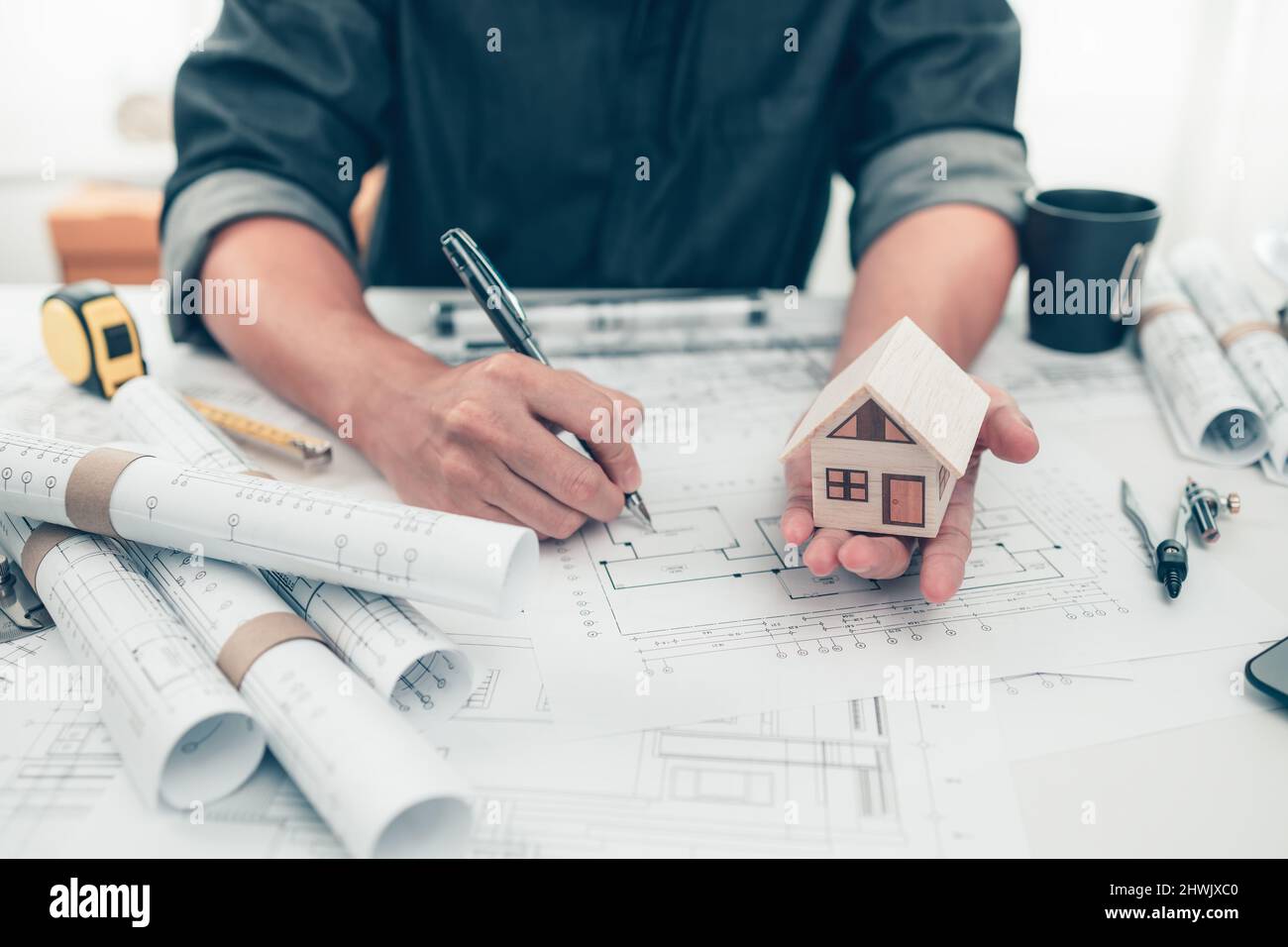 Architect engineer hands hold and show mini house model and use pen drawing on bueprint. House ...