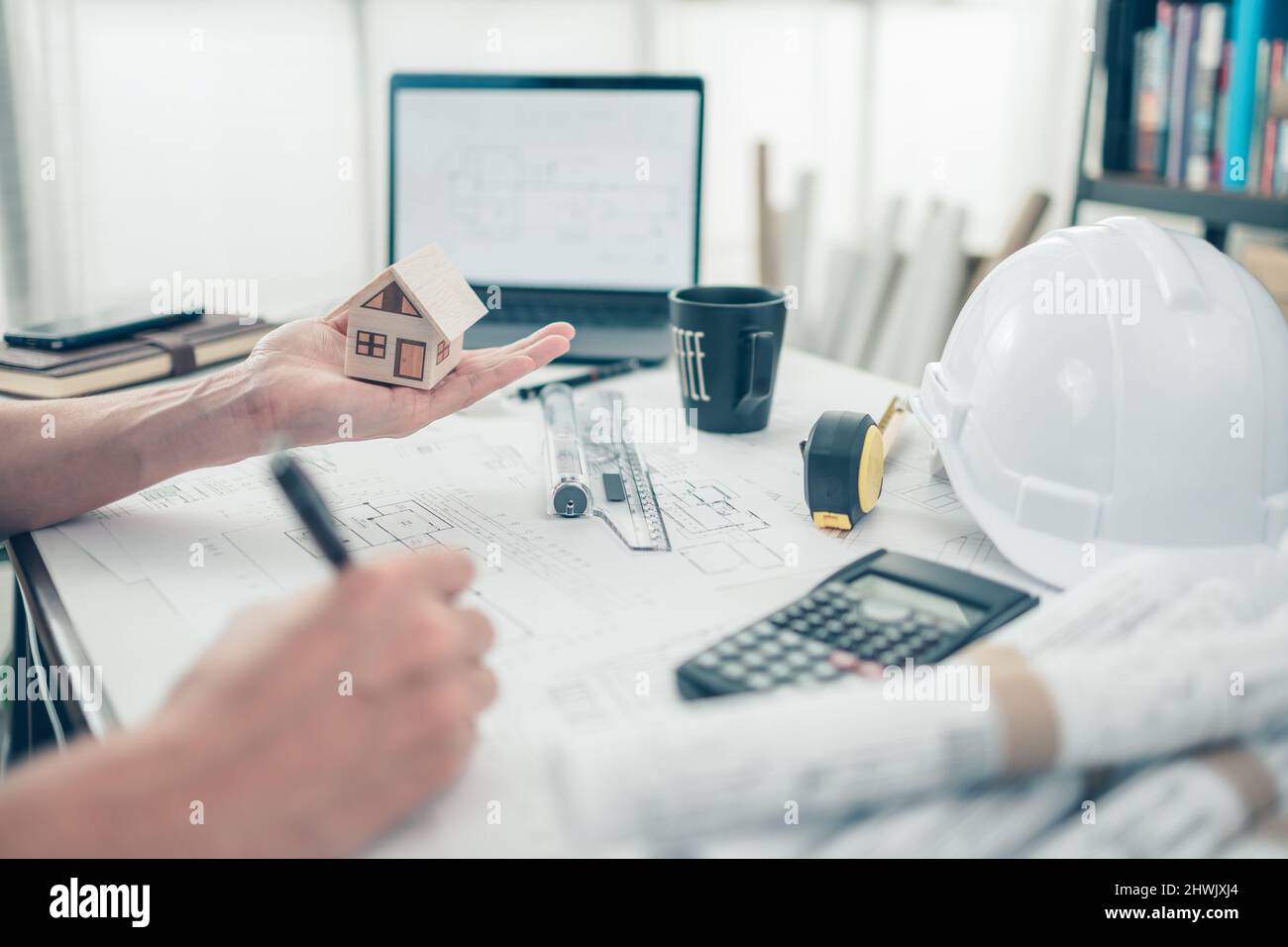 Architect engineer hands hold and show mini house model and use pen drawing on bueprint. House ...