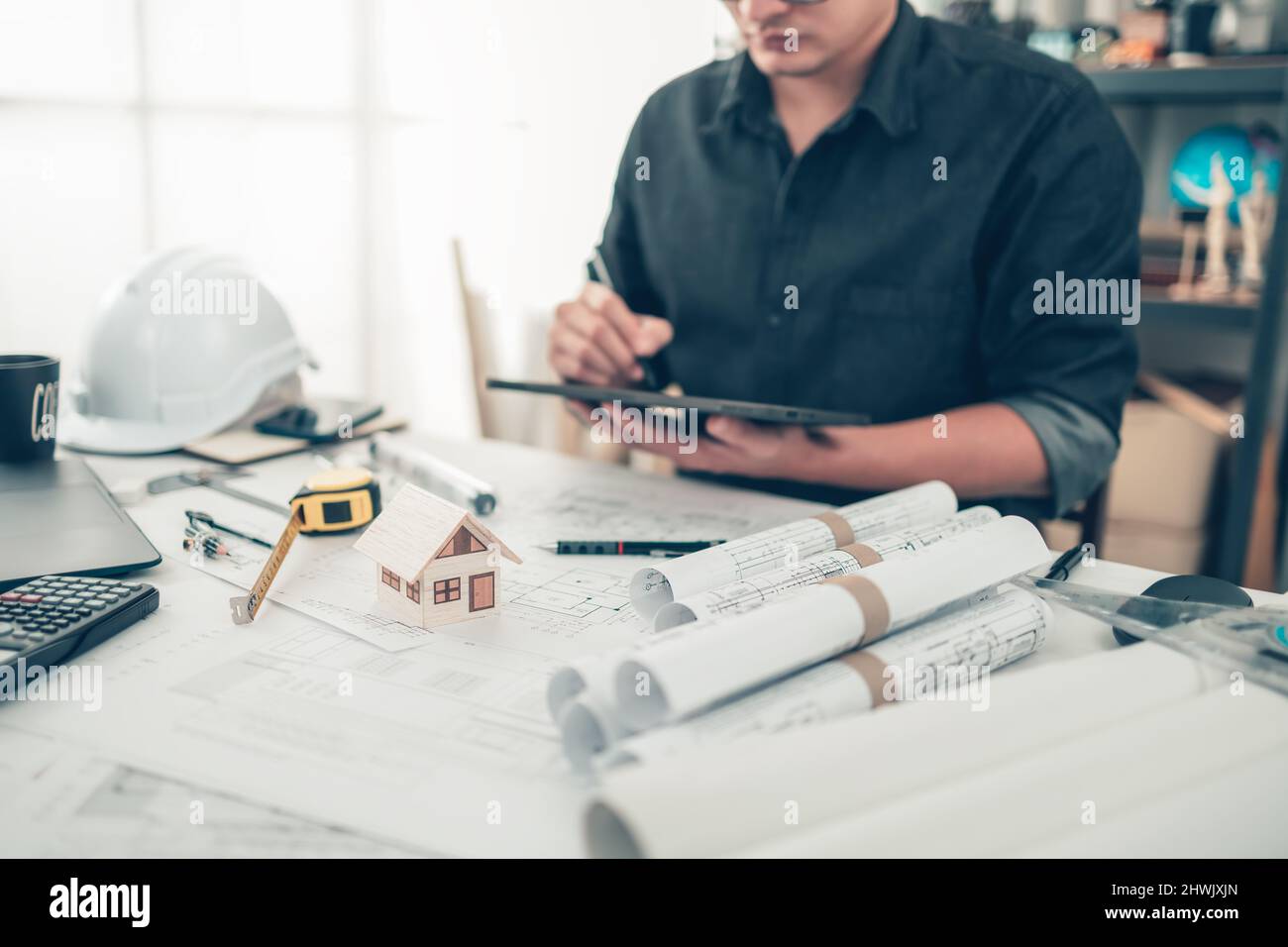Mini model house on blueprint plan while architector working on tablet ...