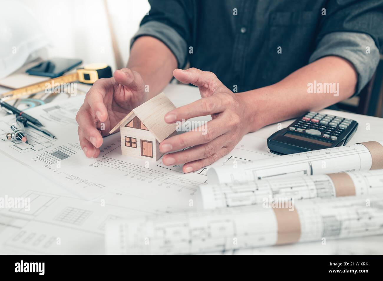 Architect engineer hands hold and protect mini house model on bueprint. Protect House, cost ...