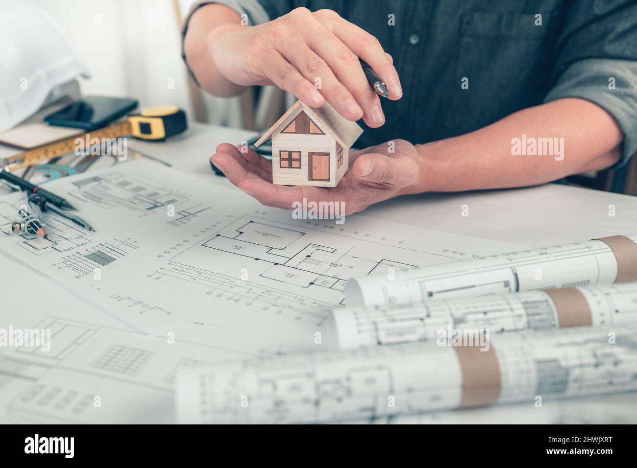Architect engineer hands hold and protect mini house model on bueprint. Protect House, cost ...