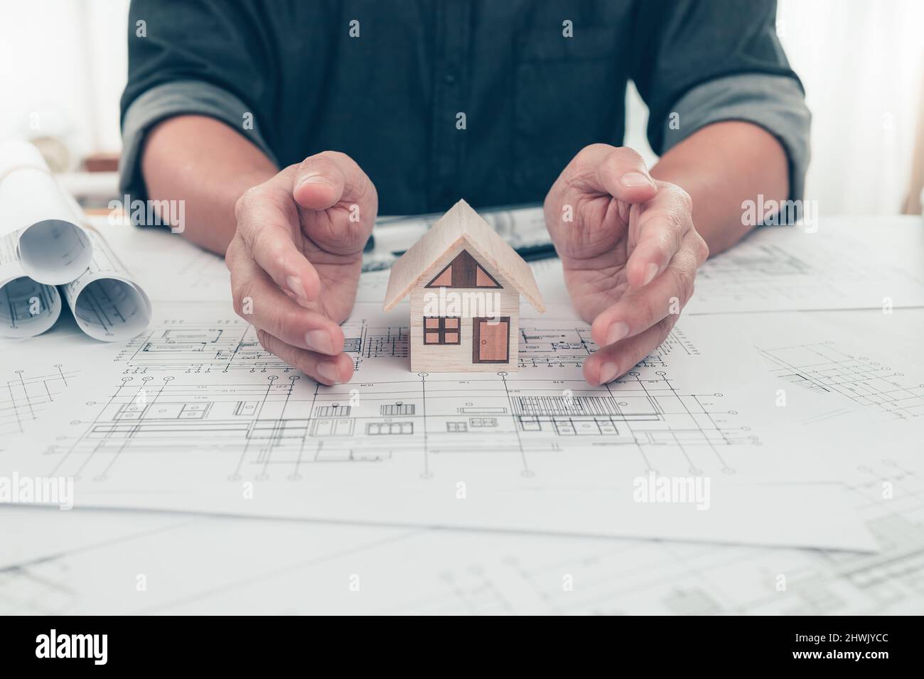 Architect engineer hands hold and protect mini house model on bueprint. Protect House, cost ...