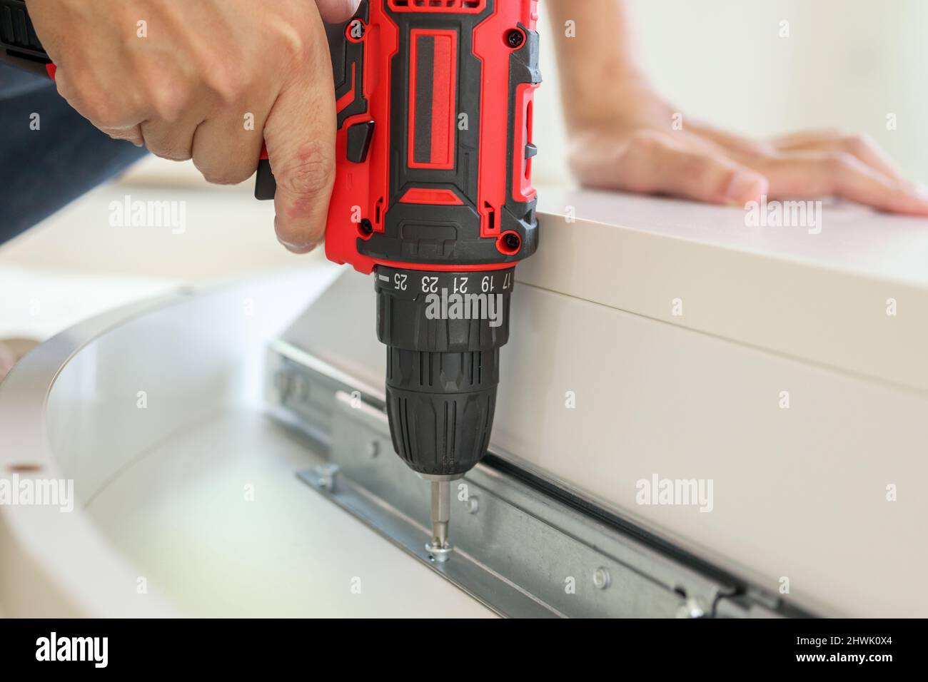 Man Assembling White Table Furniture At Home Using Cordless Screwdriver