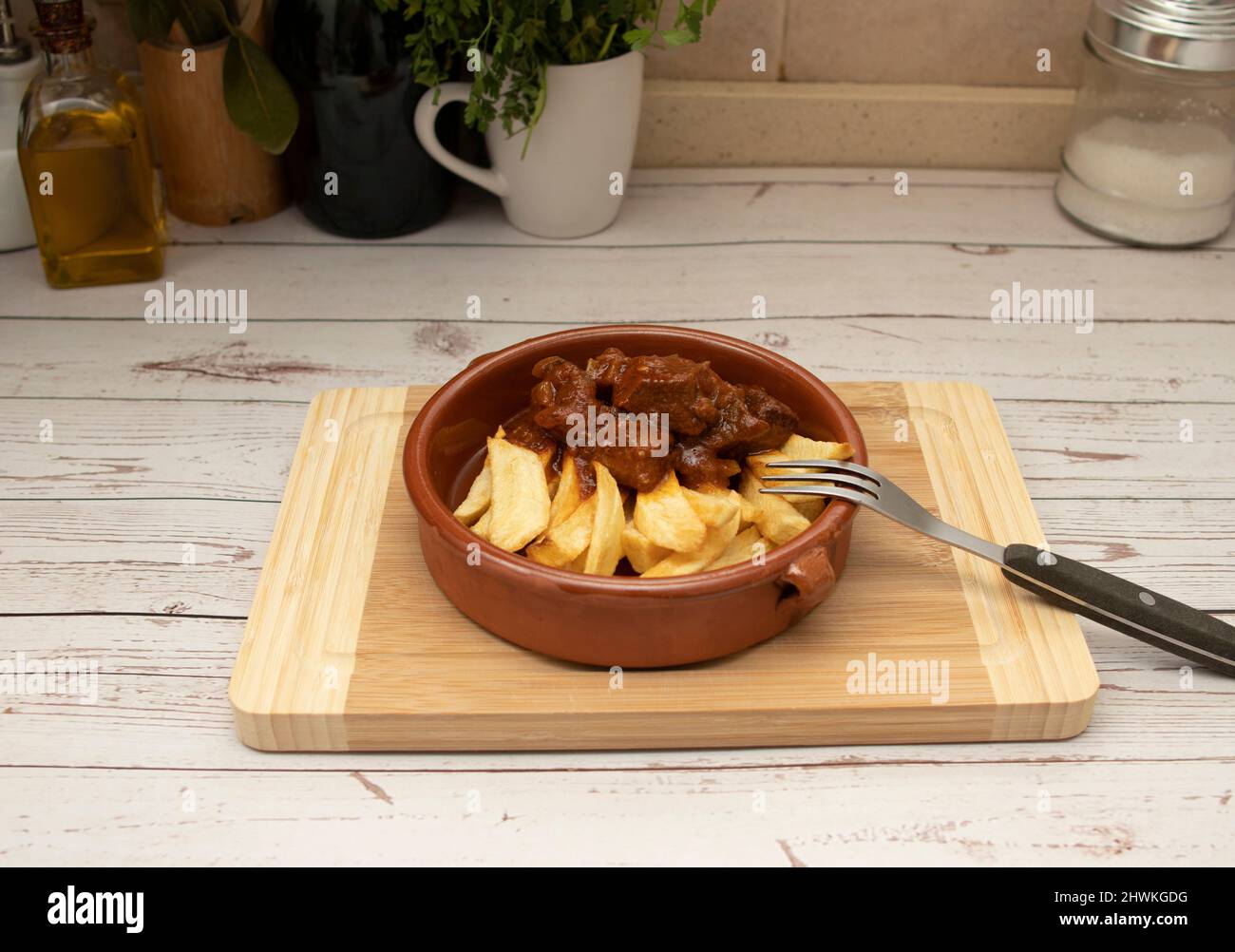 A rustic clay plate with goulash and potatoes, placed on a wooden board ...