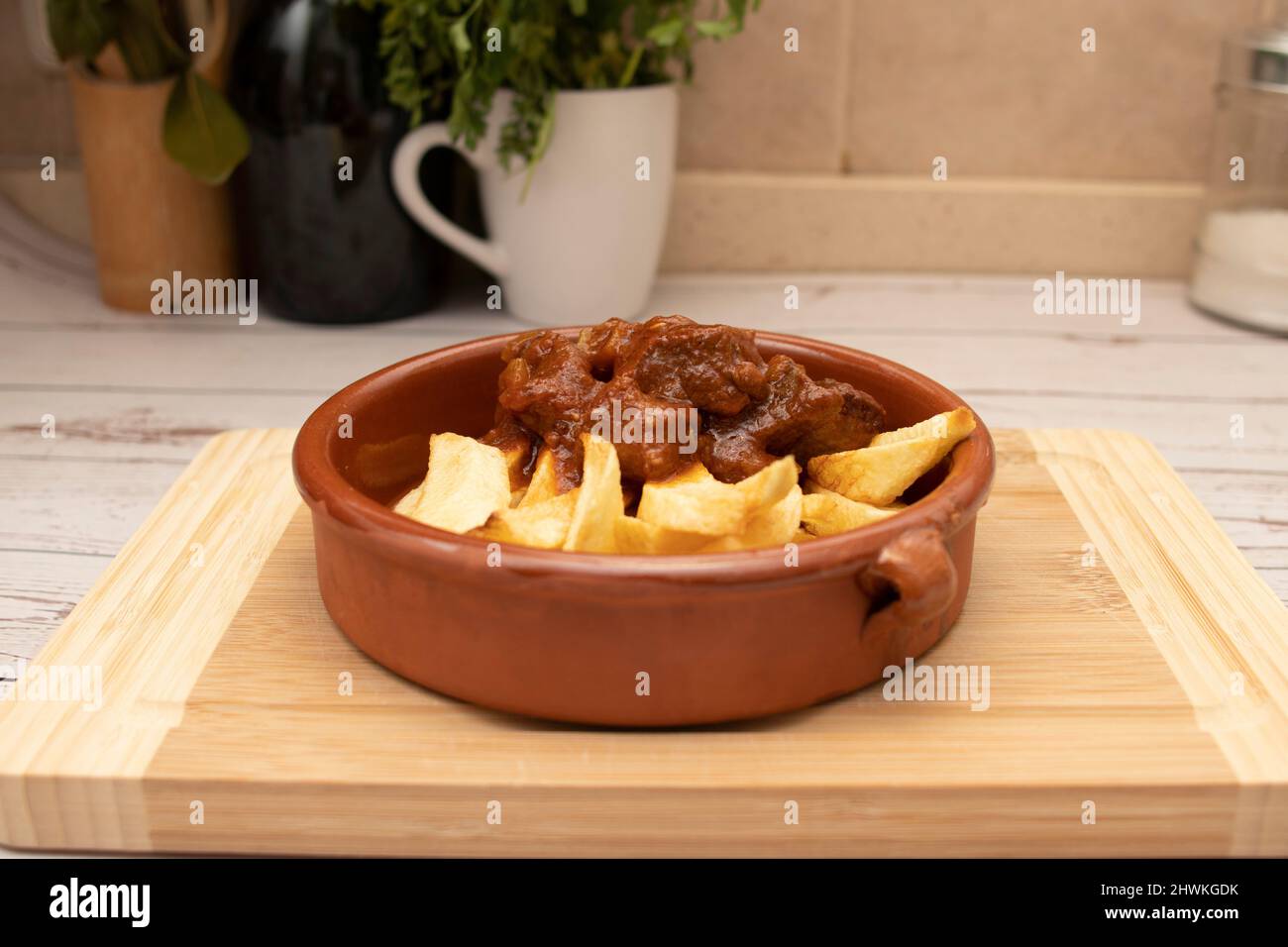 A rustic clay plate with goulash and potatoes, placed on a wooden board ...