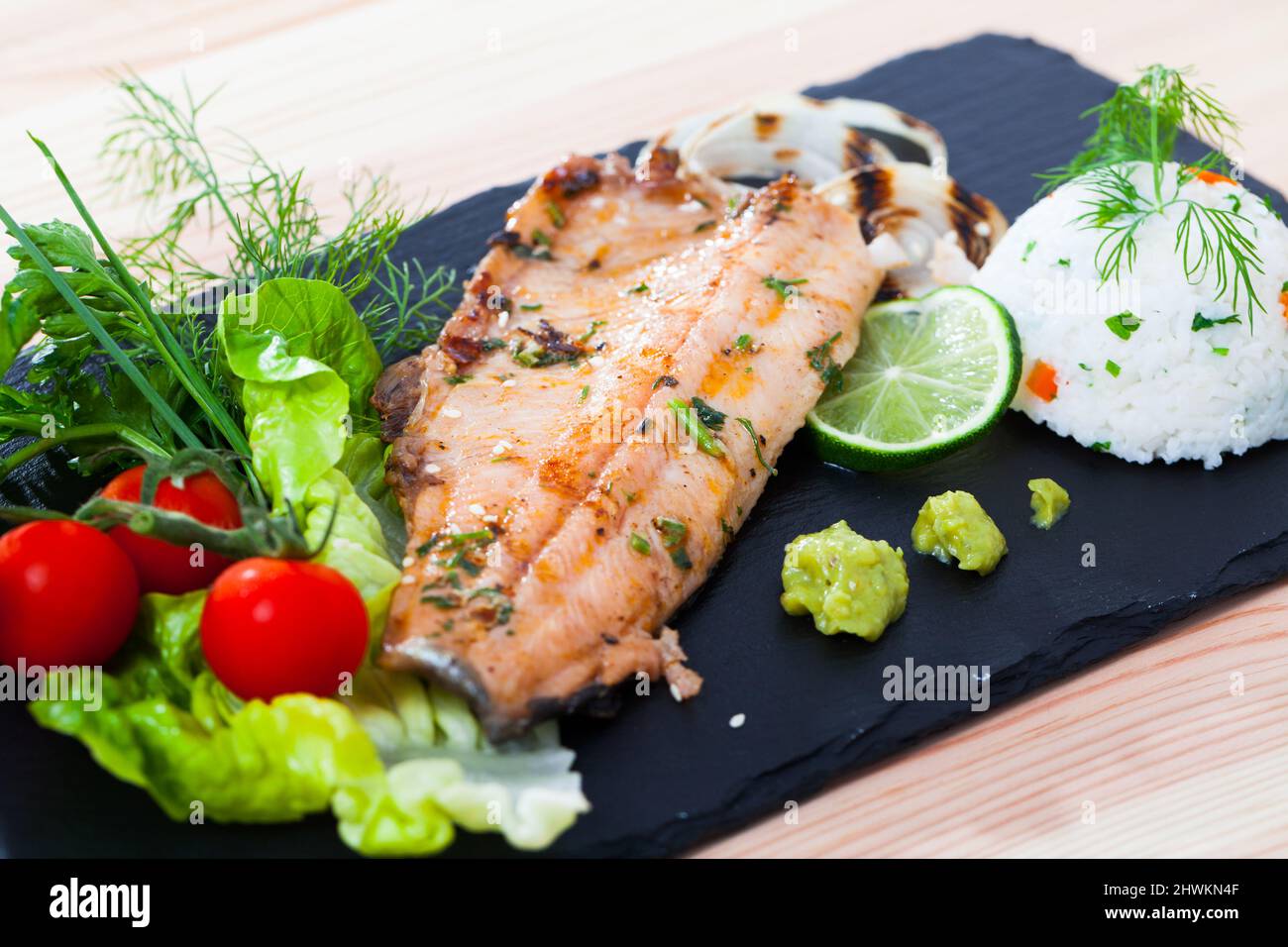 Deliciously fried trout fillet with rice and greens on black plate ...