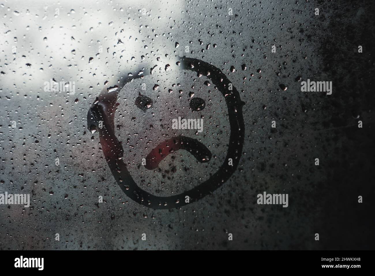 Sad smiley drawn by hand on wet fogged glass from the rain, copy space ...