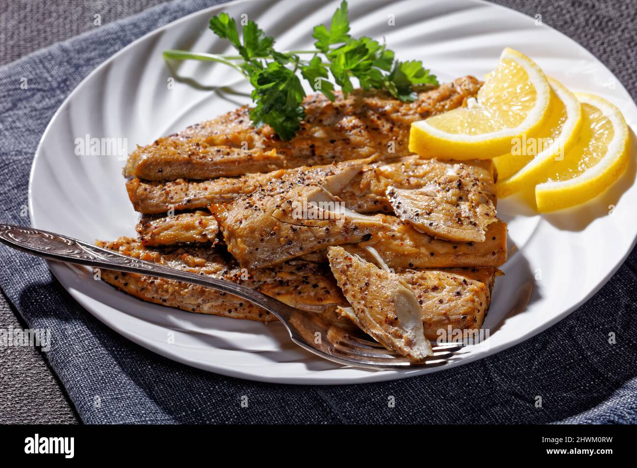 spicy mackerel fish fillets on a white plate with lemon slices and fork ...